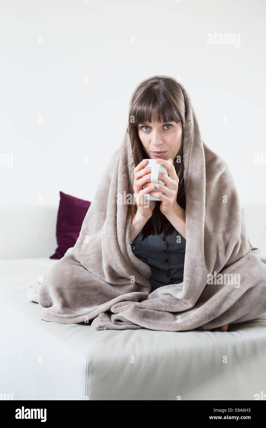 Portrait of mid adult woman covered with blanket and holding cup of tea ...
