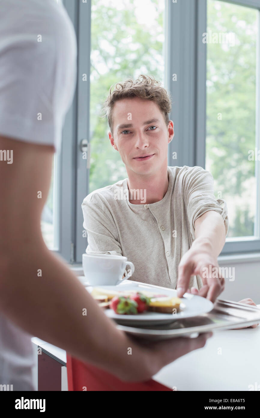 Young man offering plate with breakfast to another man, smiling Stock ...