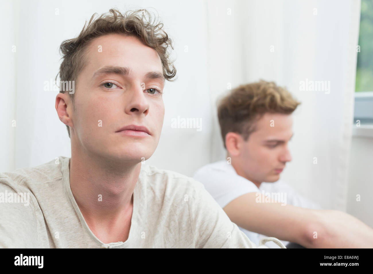Young man looking at camera while another man in background Stock Photo ...
