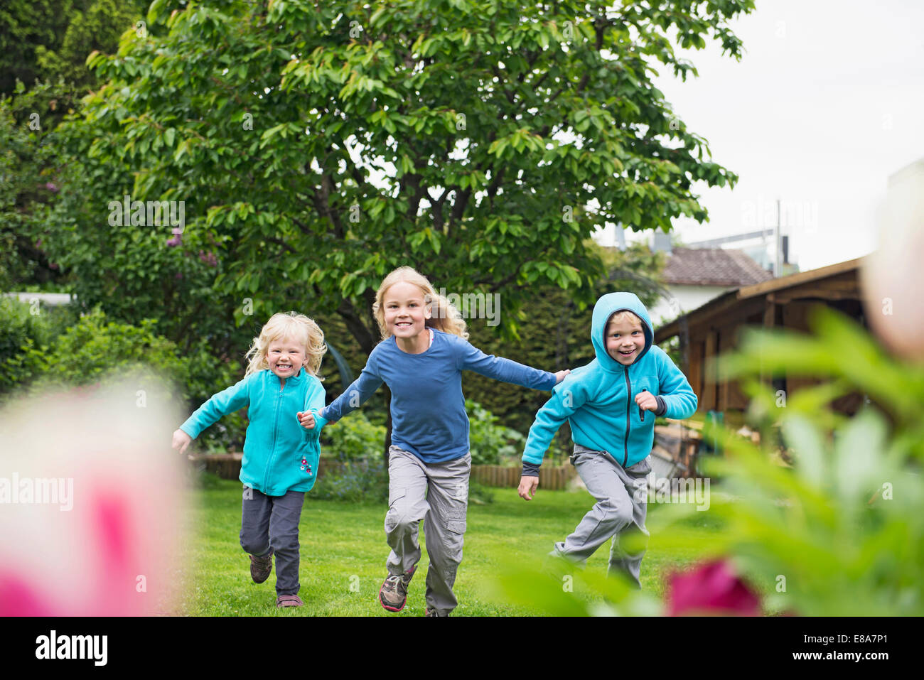 Three blonde kids running playing in garden Stock Photo - Alamy