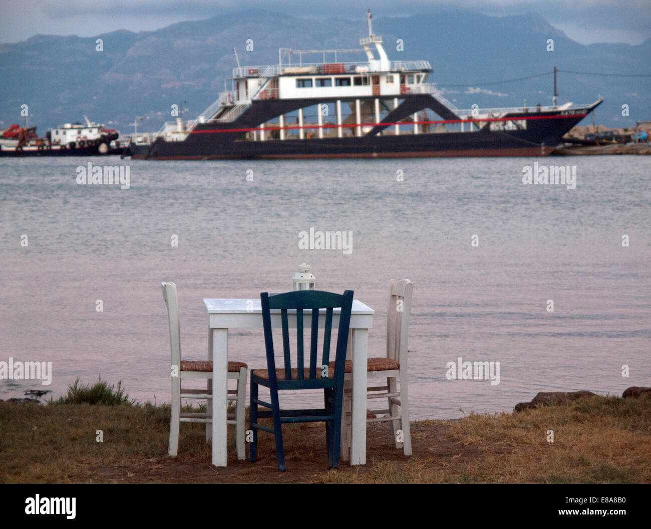 A table and chairs at the water's edge in the harbor town on the Greek ...