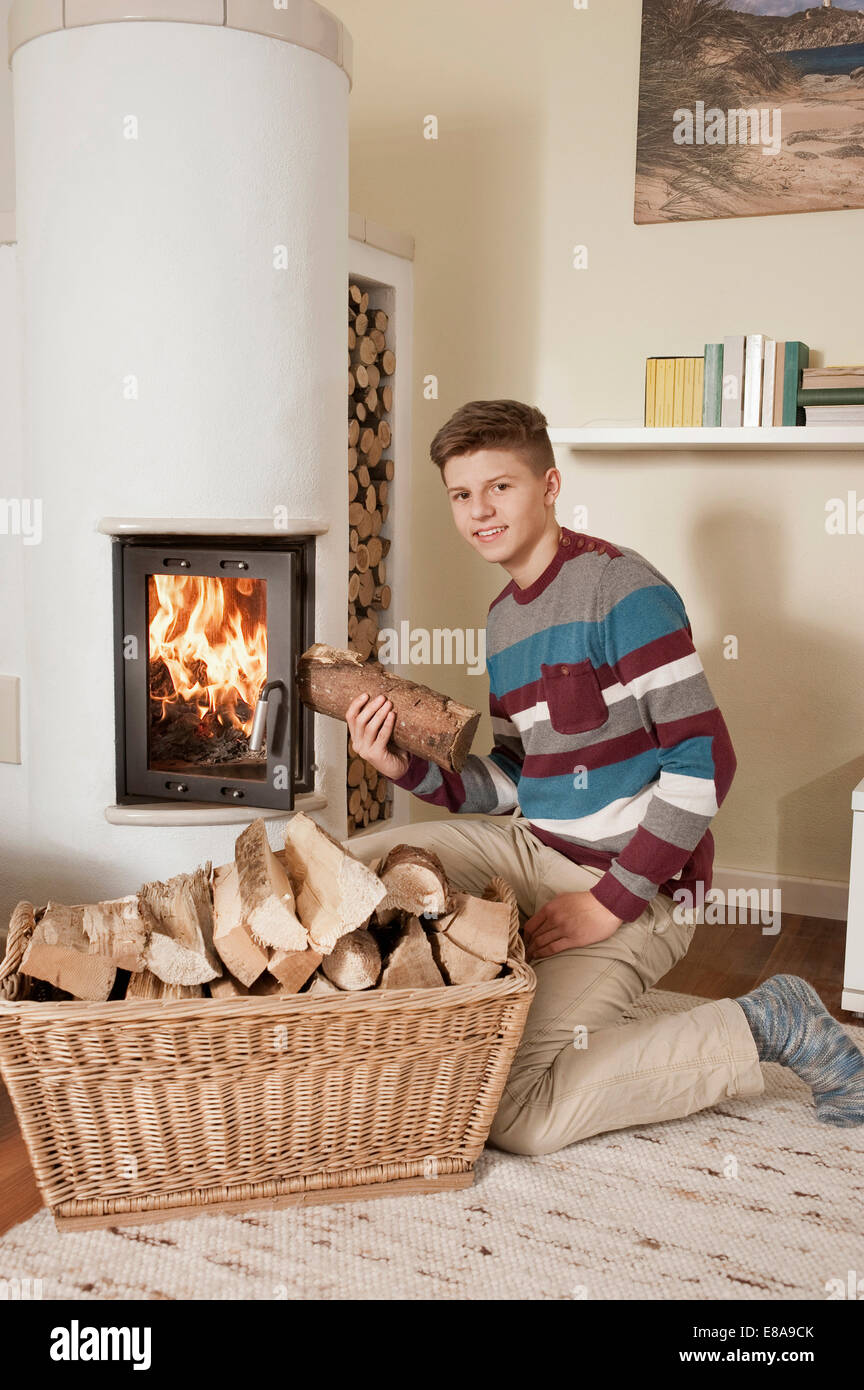 Teenage boy with log in front of fireside Stock Photo - Alamy