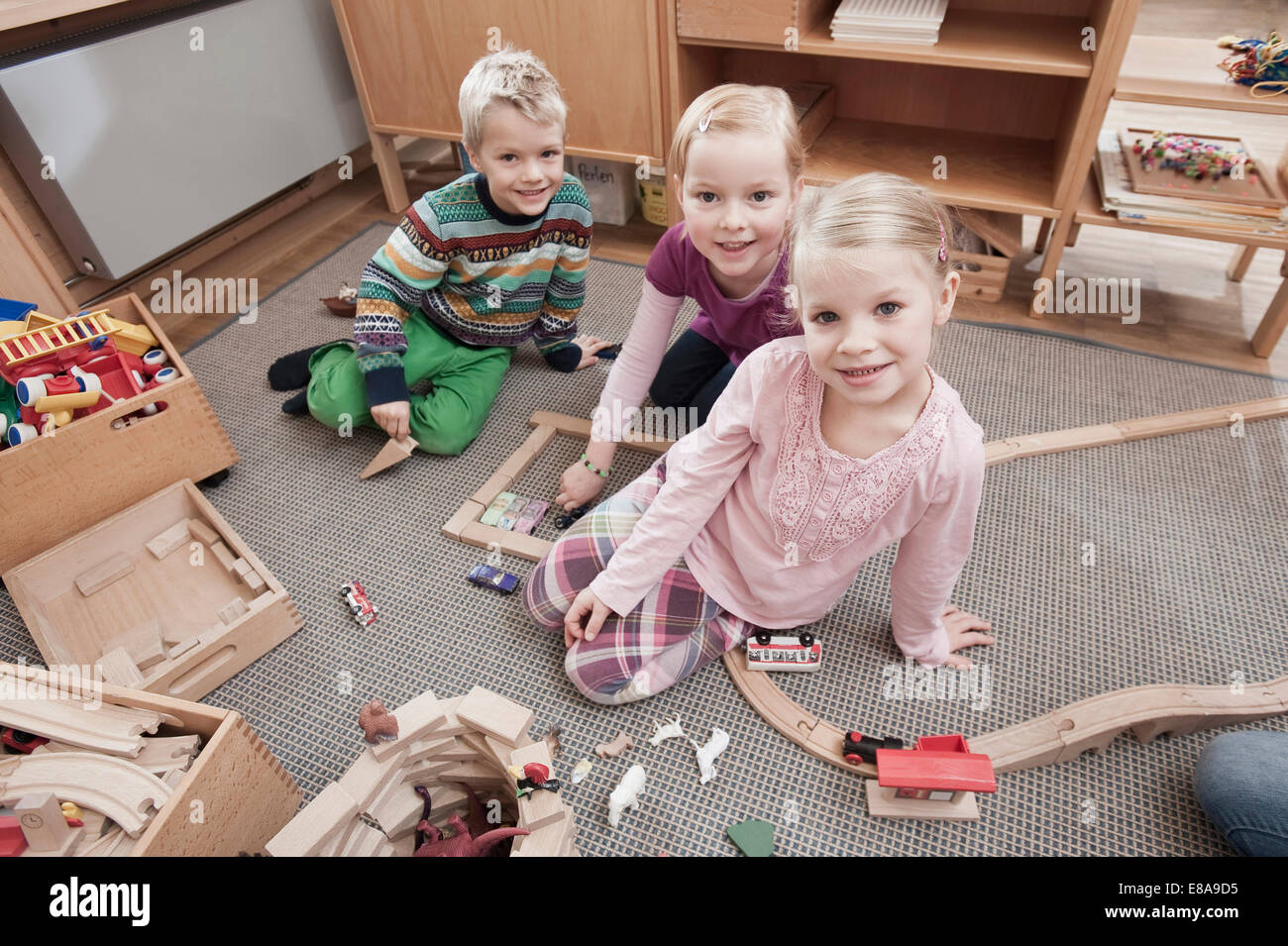 Three little children with wooden building bricks in her kindergarten ...