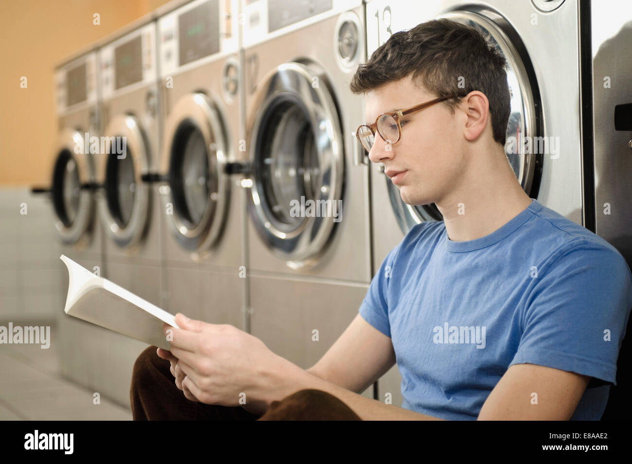 Young man reading book in laundry Stock Photo - Alamy