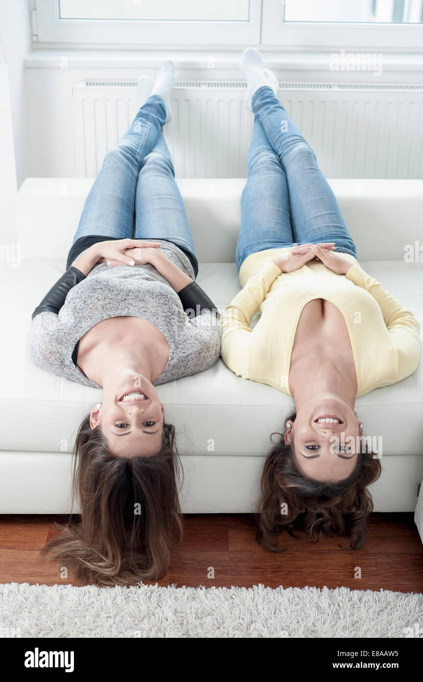 Two female friends lying with heads first side by side on couch at home ...