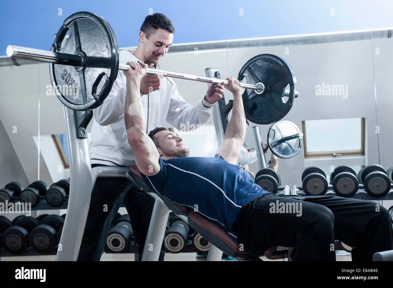 Coach supporting man in gym doing weight training Stock Photo - Alamy