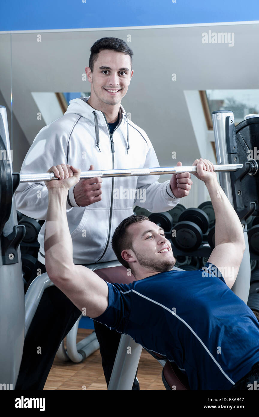 Coach supporting man in gym doing weight training Stock Photo - Alamy