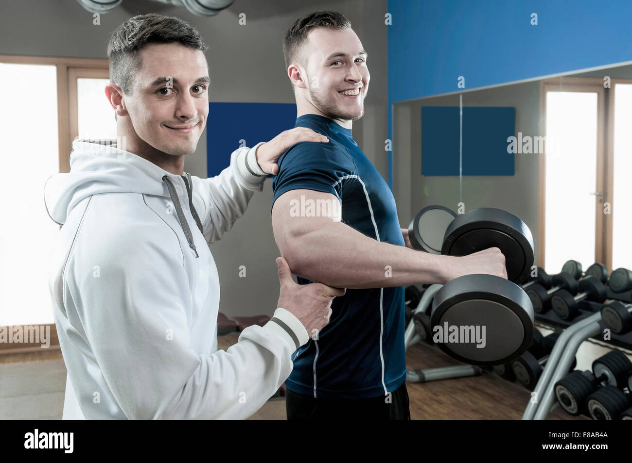Coach supporting man in gym doing weight training Stock Photo - Alamy
