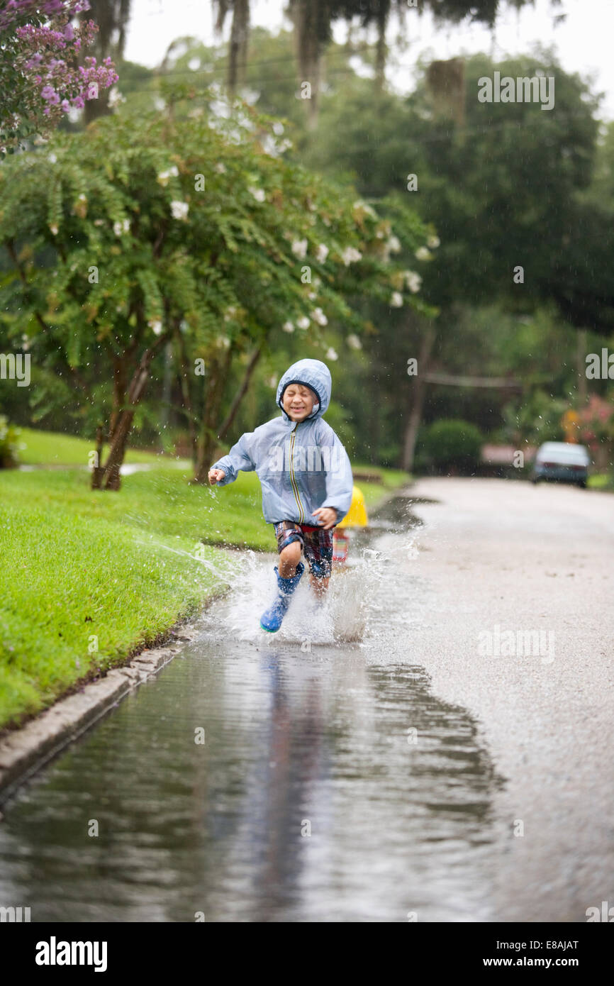 Boy in rubber boots running and splashing in rain puddle Stock Photo ...