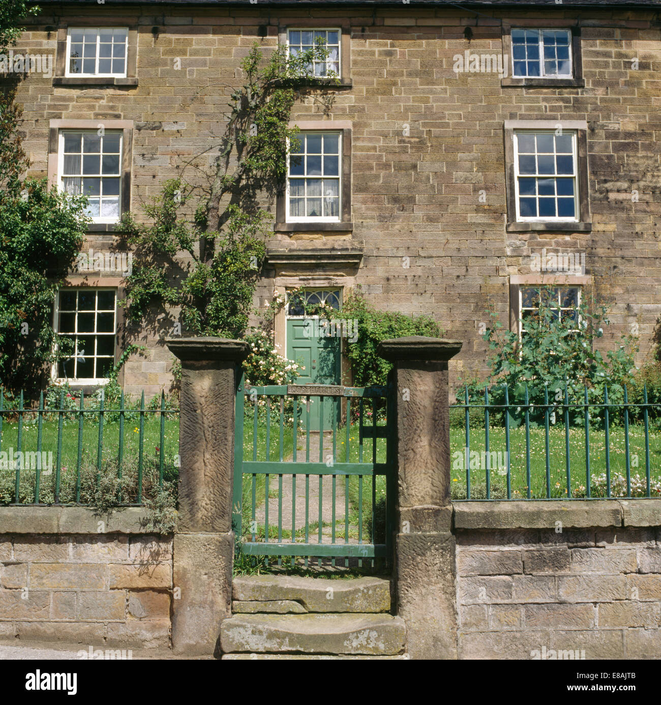 Green painted gate with stone pillars and iron railings in front of ...