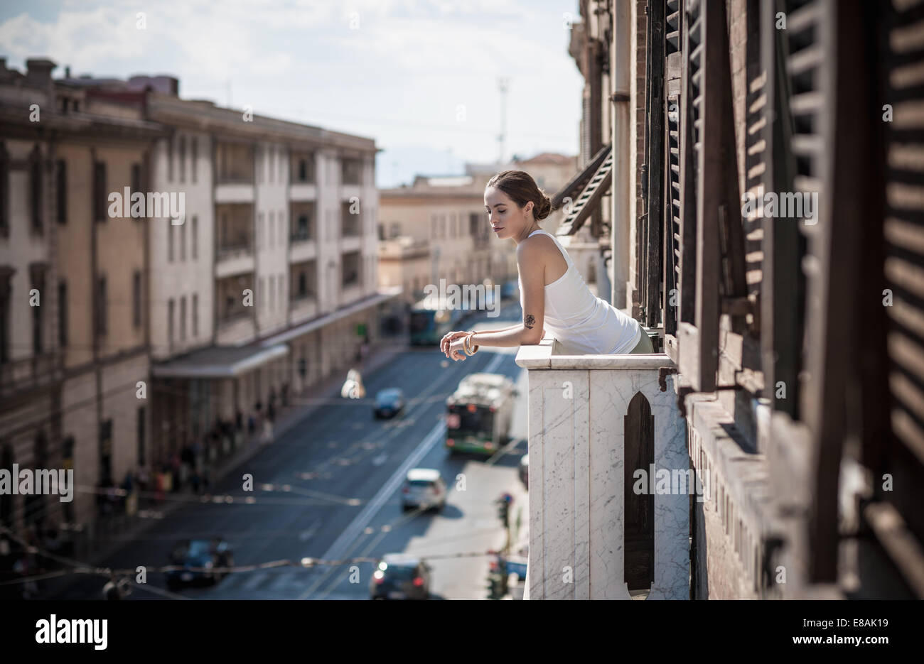Young woman looking over balcony onto street, Castiadas, Sardinia ...