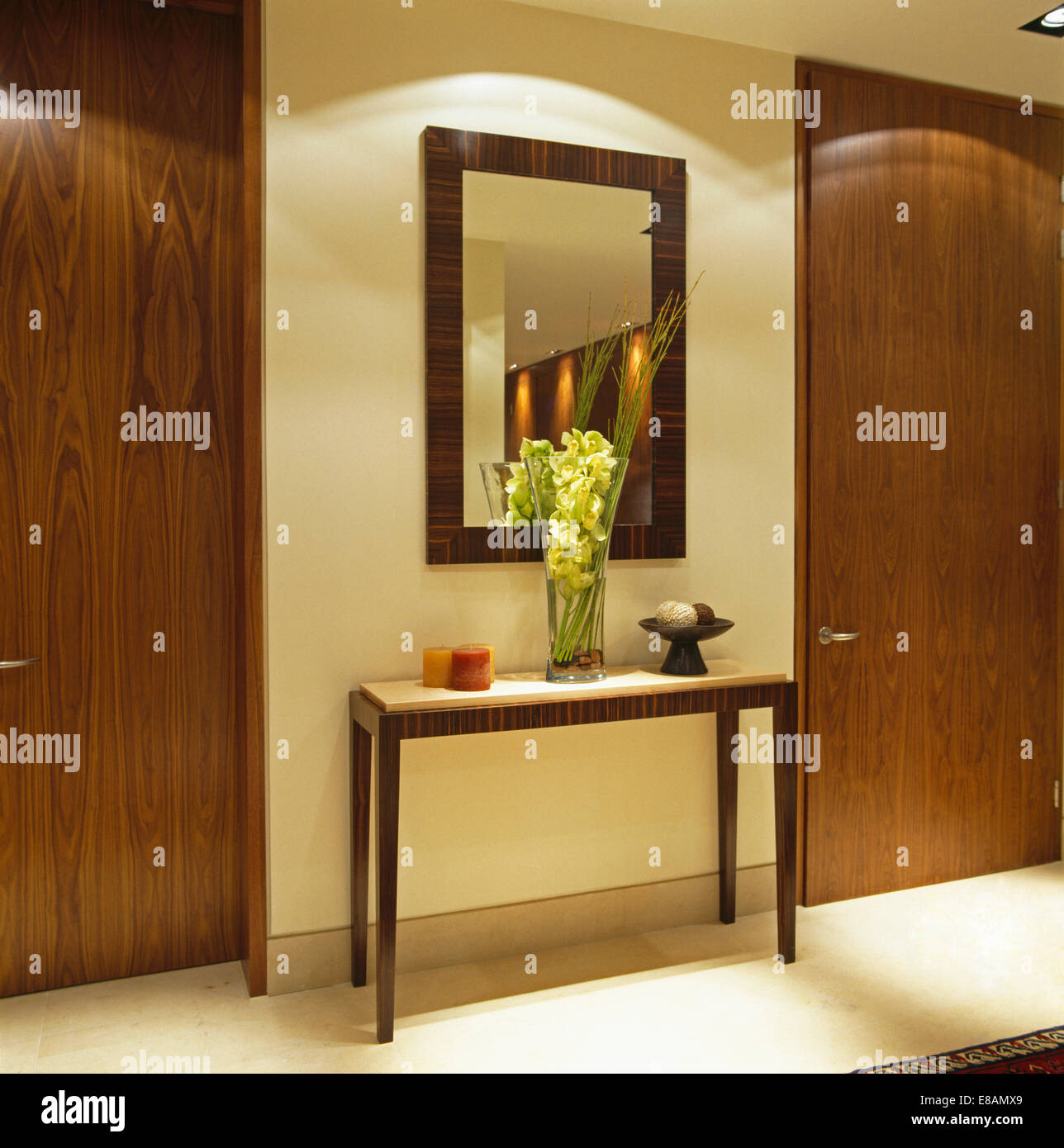 Rectangular mirror above console table with vase of cream gladioli in ...