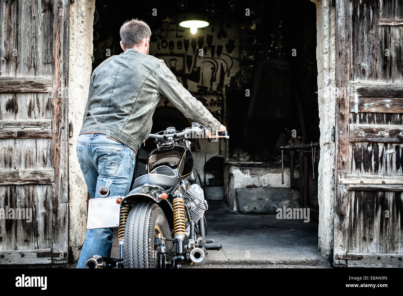Mid adult man pushing motorcycle into barn Stock Photo - Alamy
