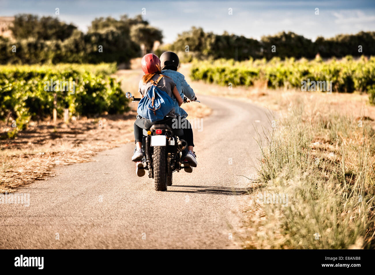 Rear view of mid adult couple riding motorcycle on winding rural road ...