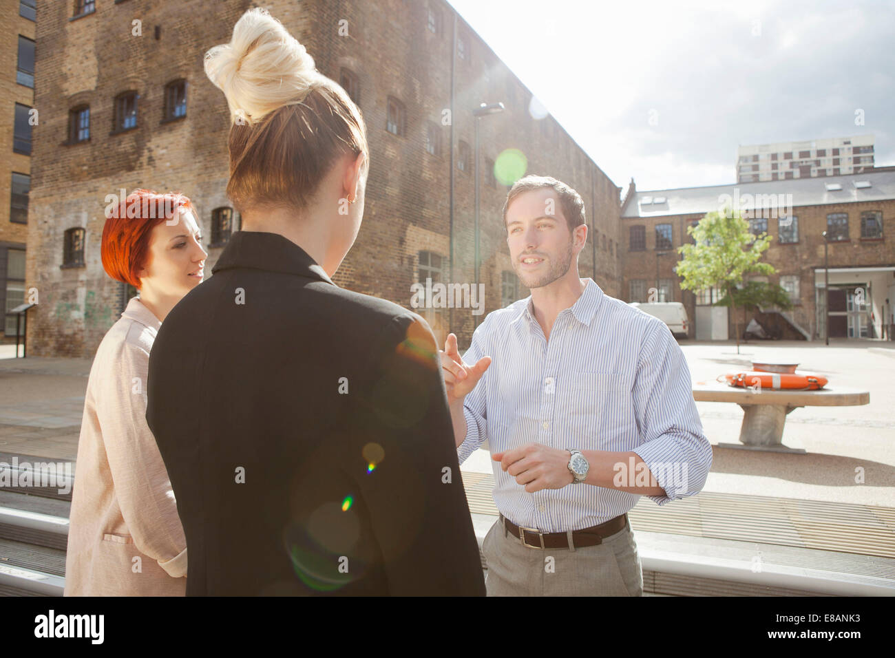 Three young people talking, building in background, East London, UK ...