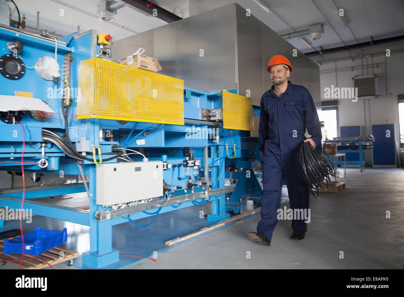 Worker carrying reel of cable in industrial plant Stock Photo - Alamy