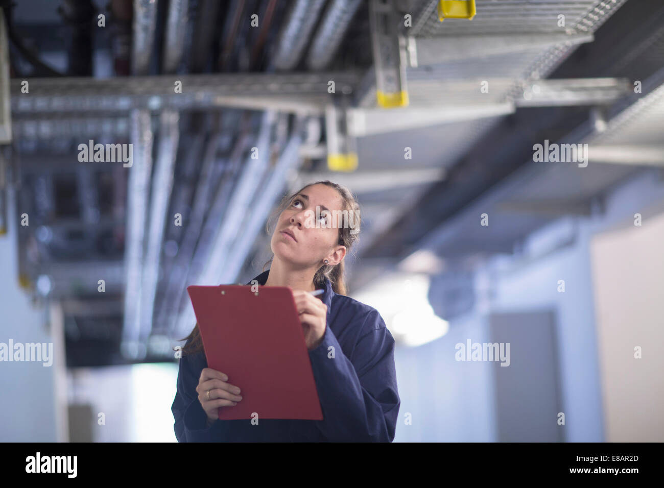 Female engineer with clipboard checking industrial piping in factory ...
