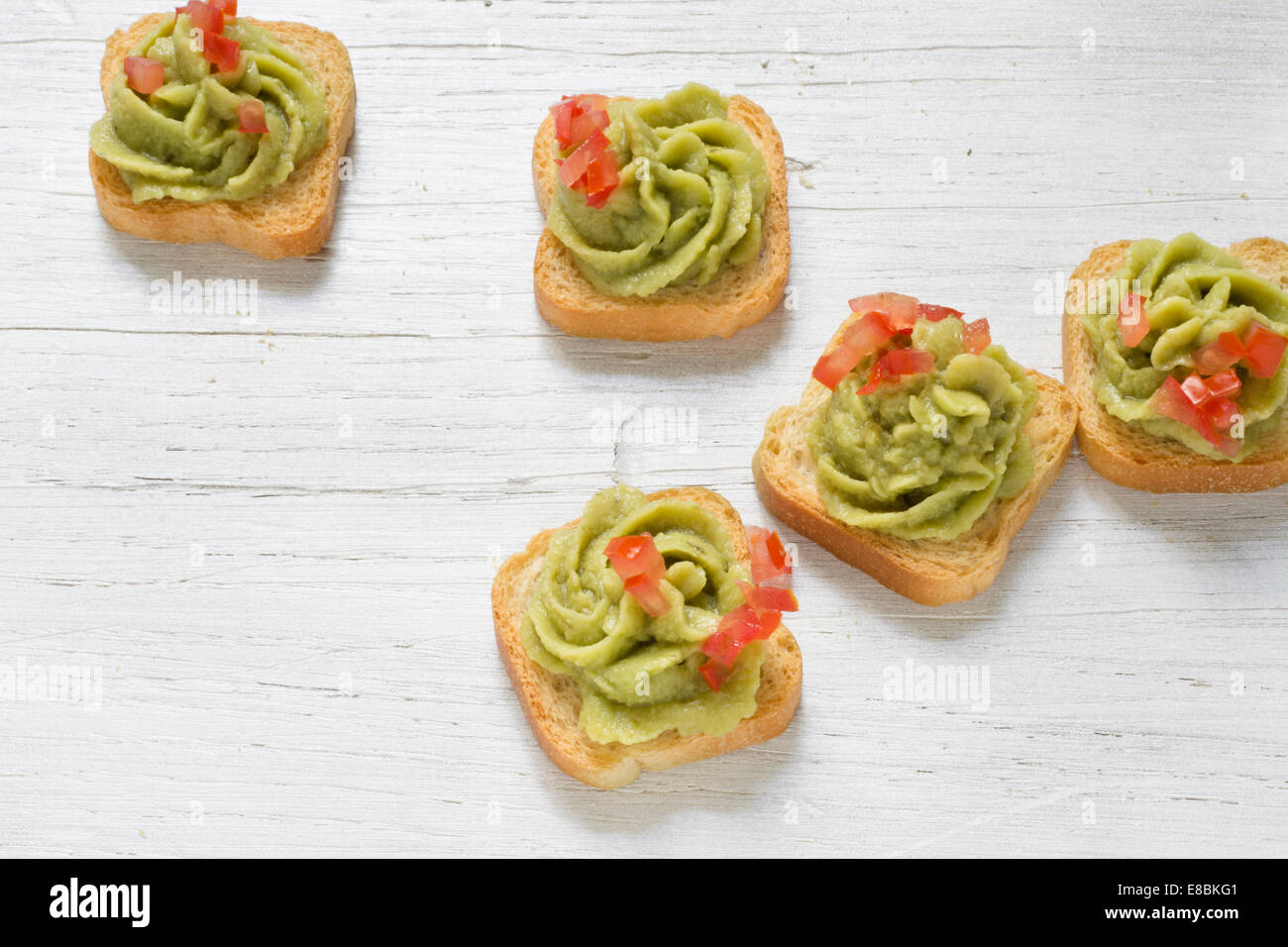 Mini-toast, decorated with guacamole, chopped tomato, white wooden ...