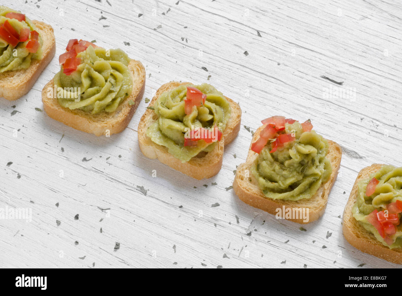Mini-toast, decorated with guacamole, chopped tomato, white wooden ...