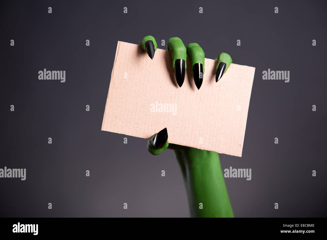 Green monster hand with sharp nails holding blank piece of cardboard ...