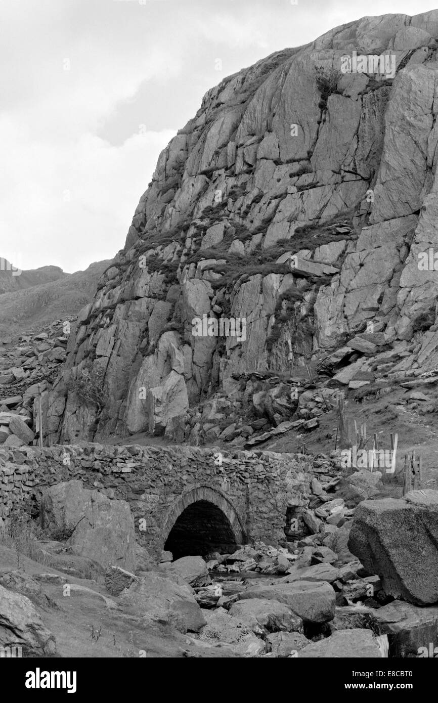 small stone bridge beneath rocky mountain outcrop over river in rural ...