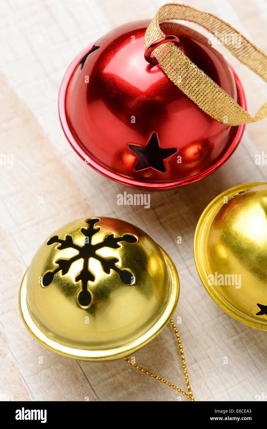 Closeup of three jingle bells on a white wood table. Two gold bells and ...