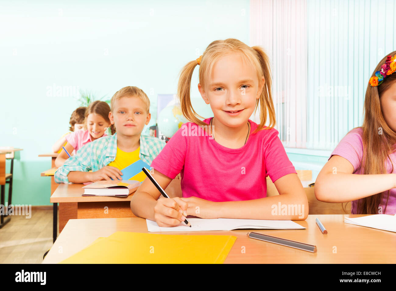 Kids sitting at table in classroom and writing Stock Photo - Alamy