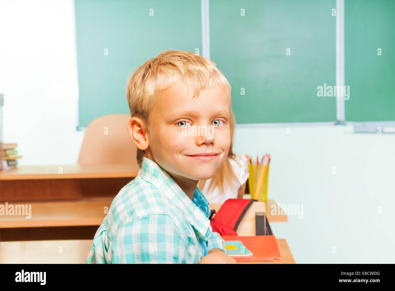 Smiling boy sits at desk with blackboard behind Stock Photo - Alamy