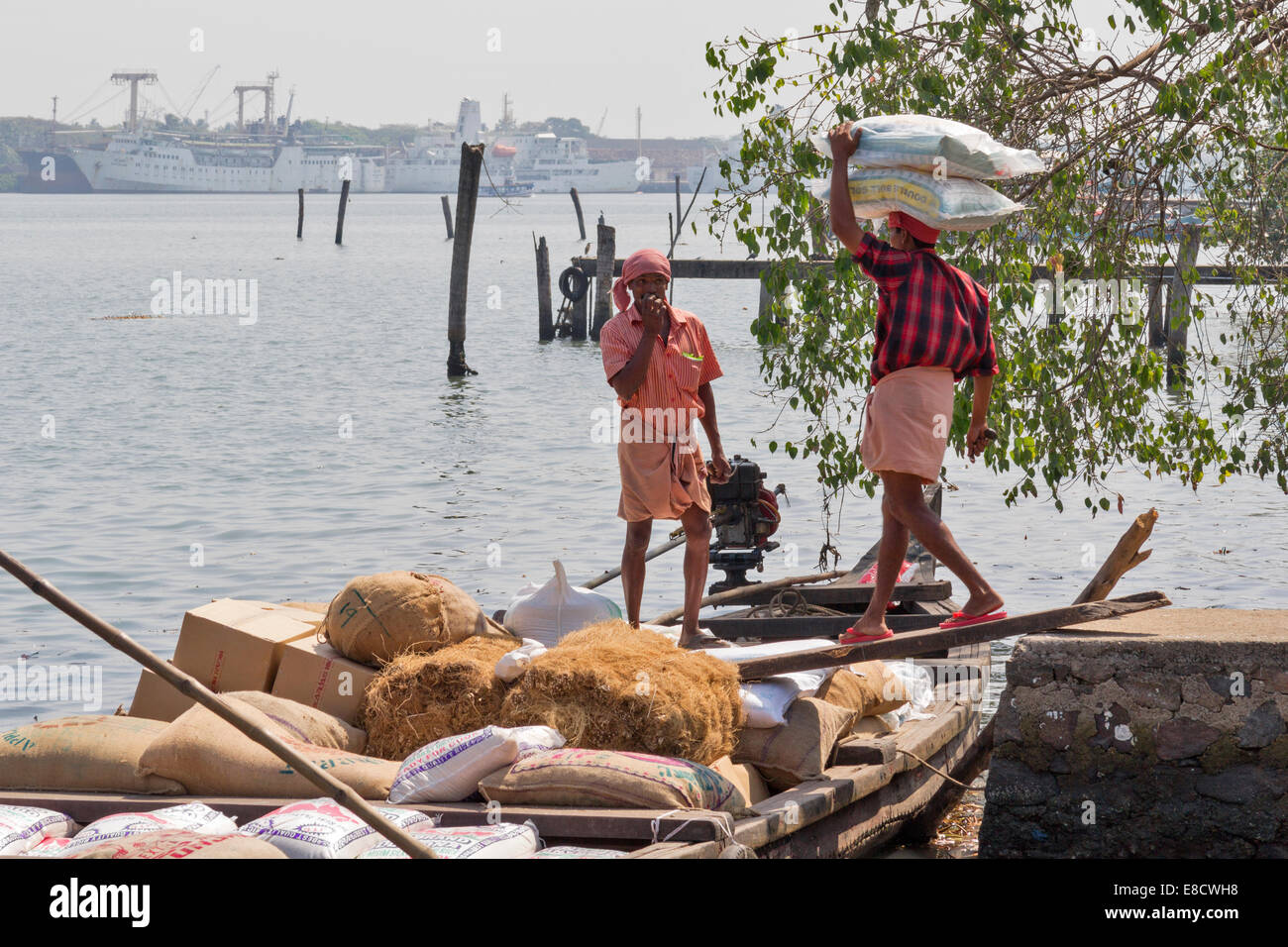 TWO MEN LOADING AN OLD WOODEN BOAT WITH HEAVY SACKS OF FOOD IN PORT ...