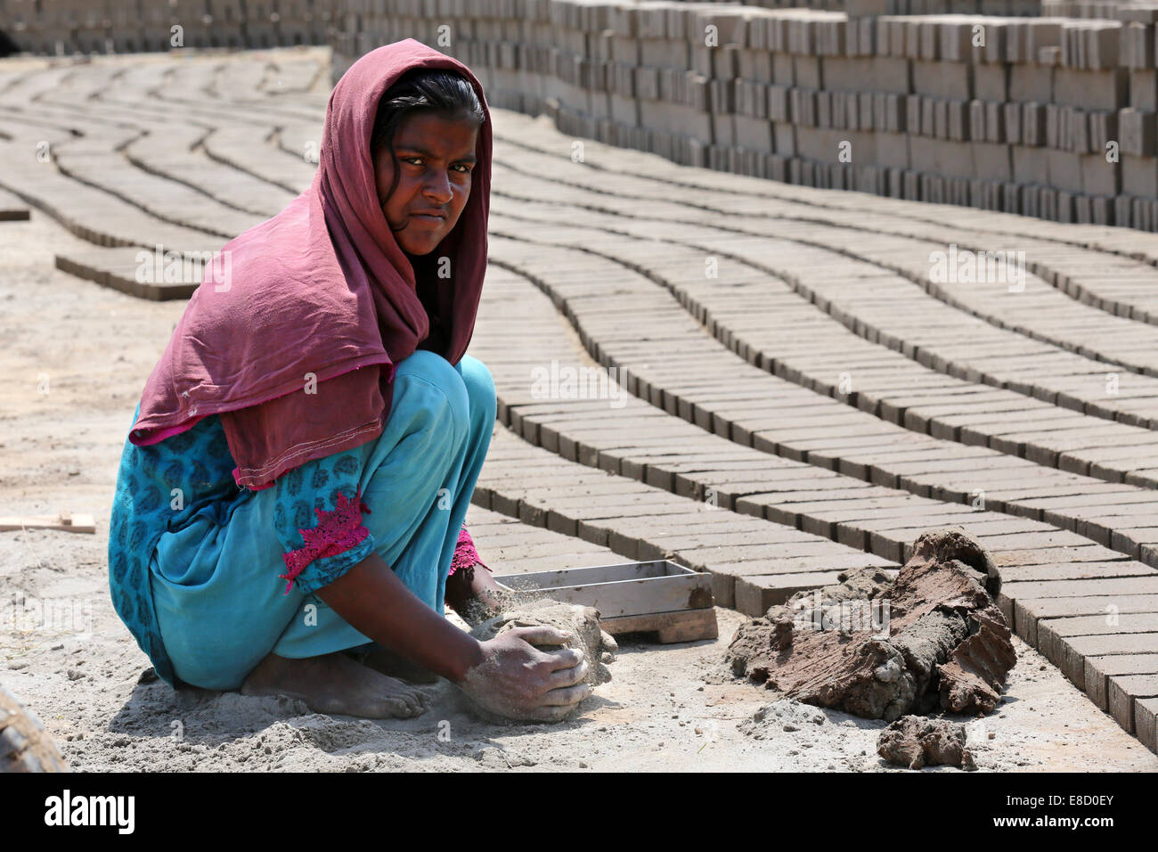 female brickyard worker (16 years) form clay bricks on a field of the ...