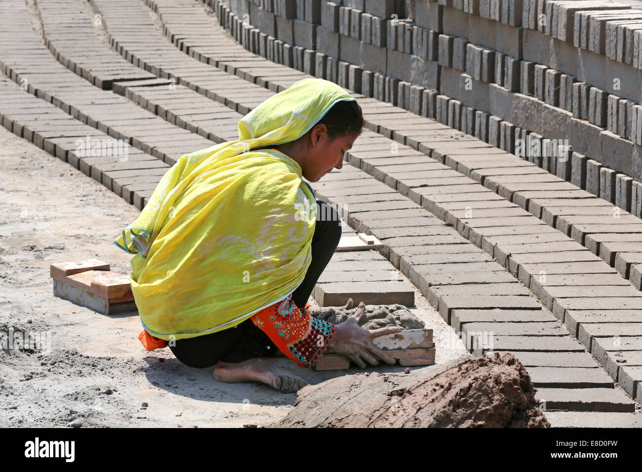 female brickyard worker (14 years old) form clay bricks on a field of ...