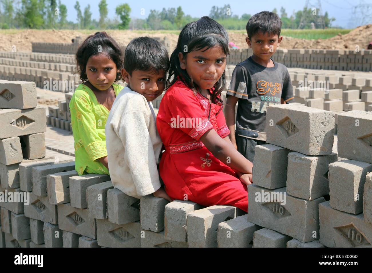 children of brickyard worker on a wall of clay bricks on a field of the ...