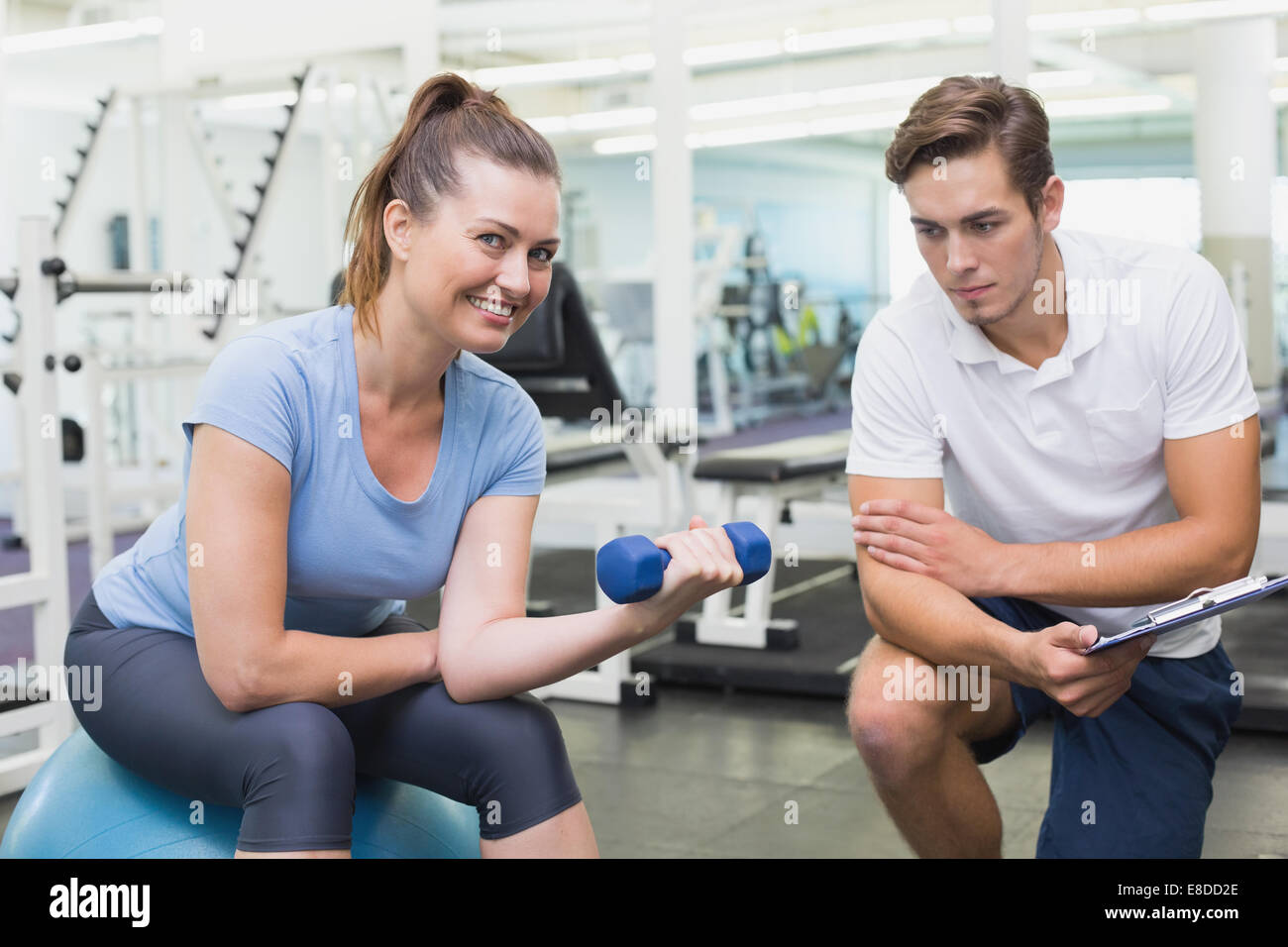 Personal trainer working with client holding dumbbell Stock Photo - Alamy
