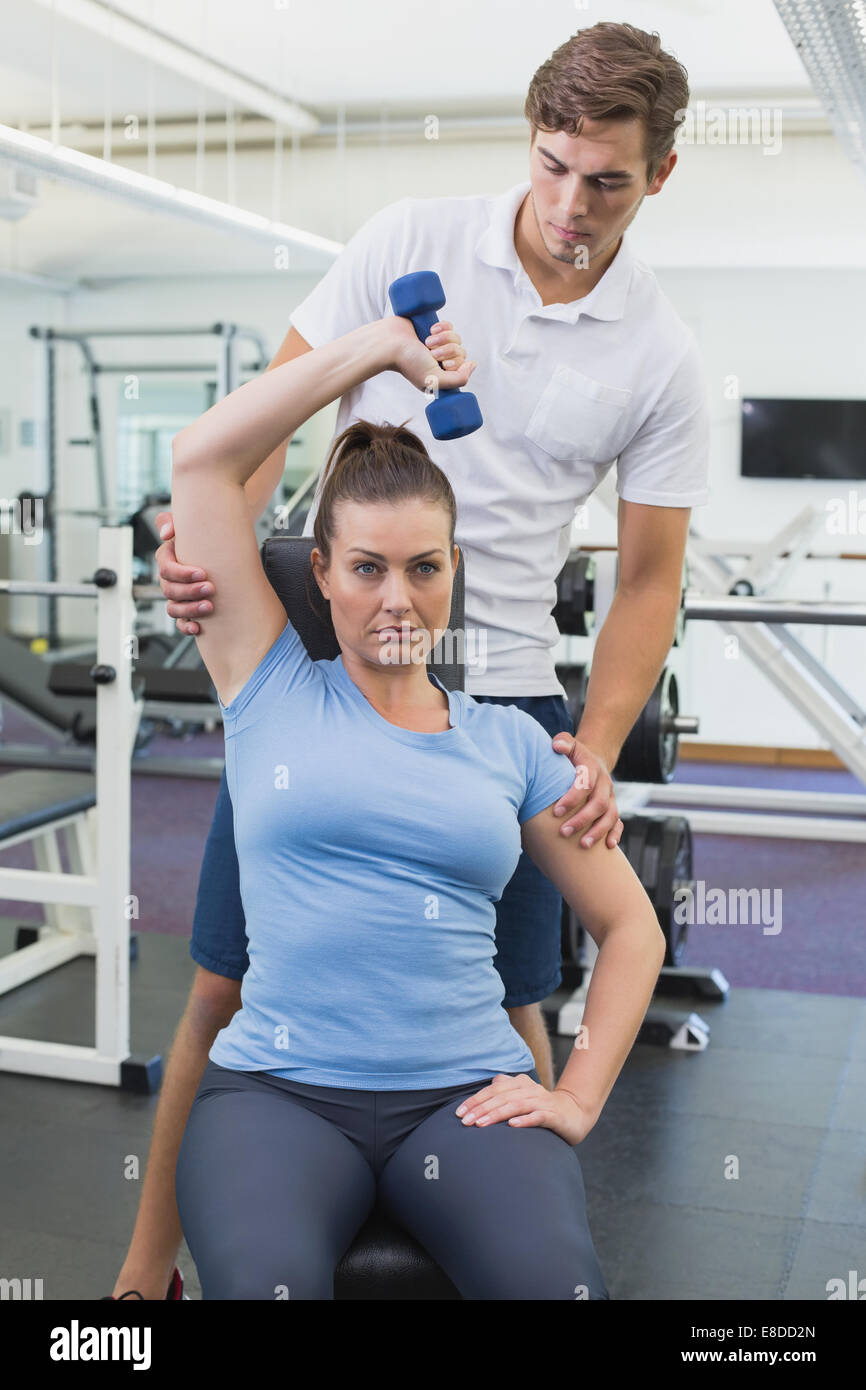 Personal trainer helping client lift dumbbell Stock Photo - Alamy