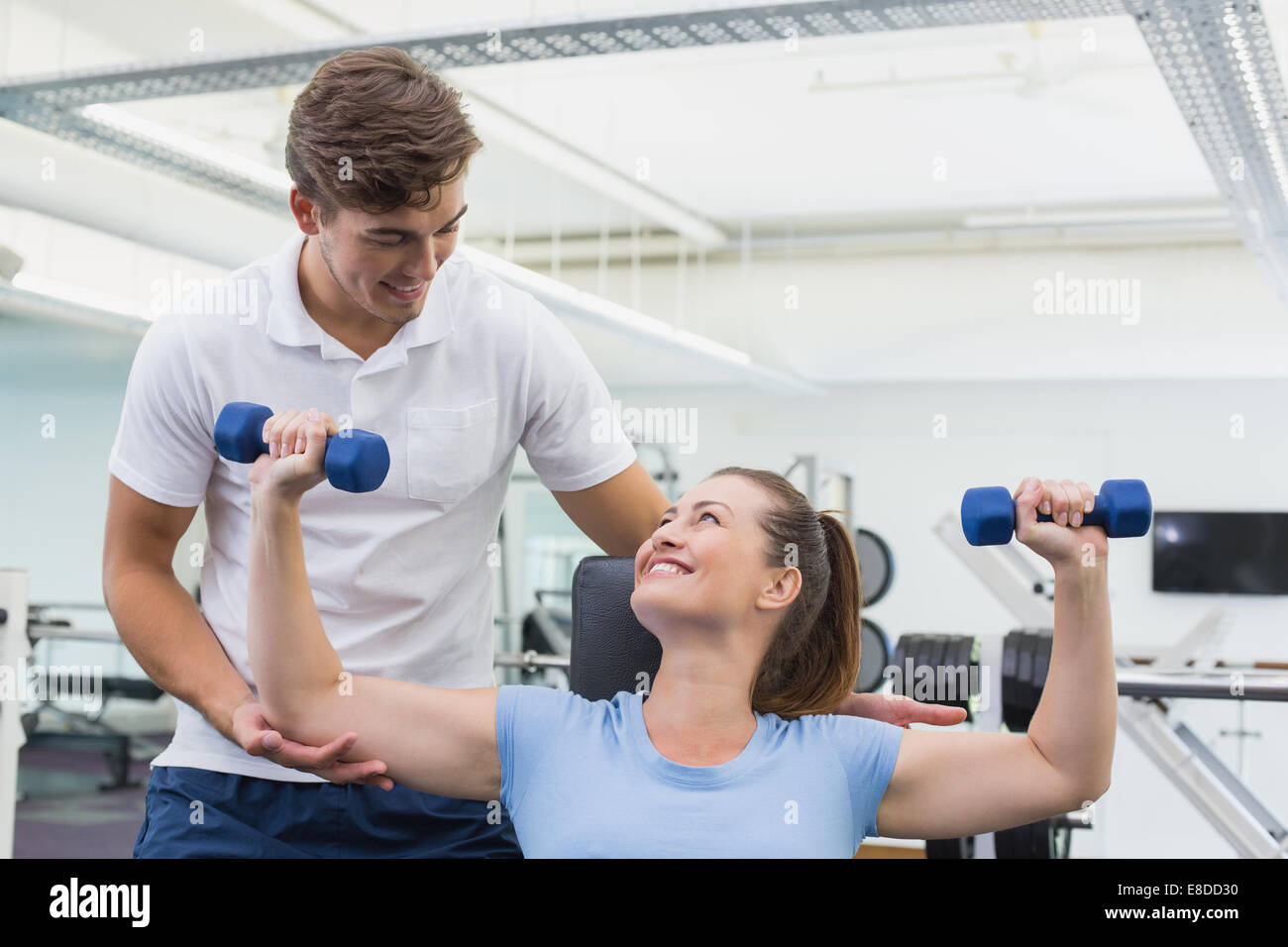 Personal trainer helping client lift dumbbell Stock Photo - Alamy