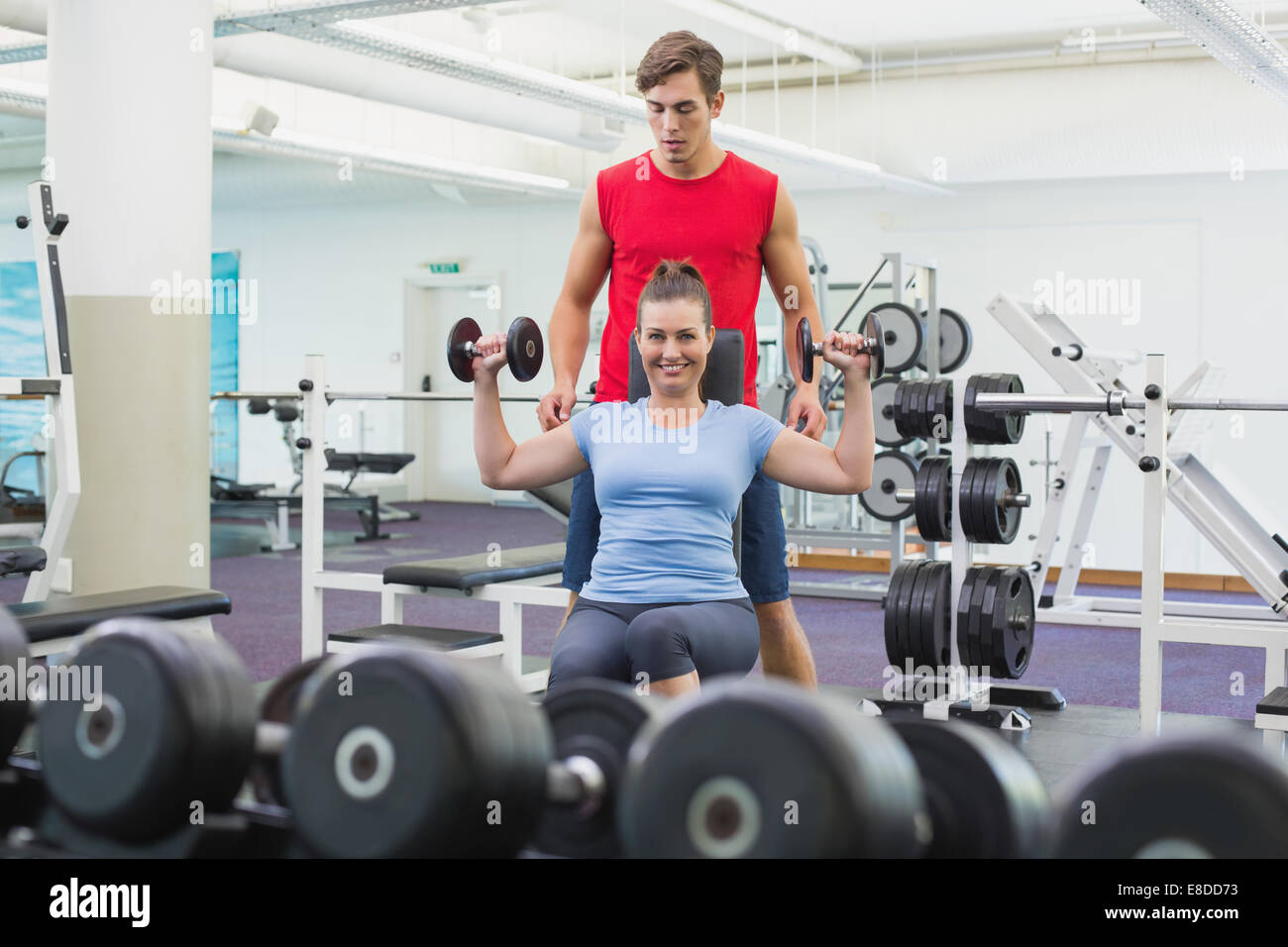 Personal trainer helping client lift dumbbells Stock Photo - Alamy