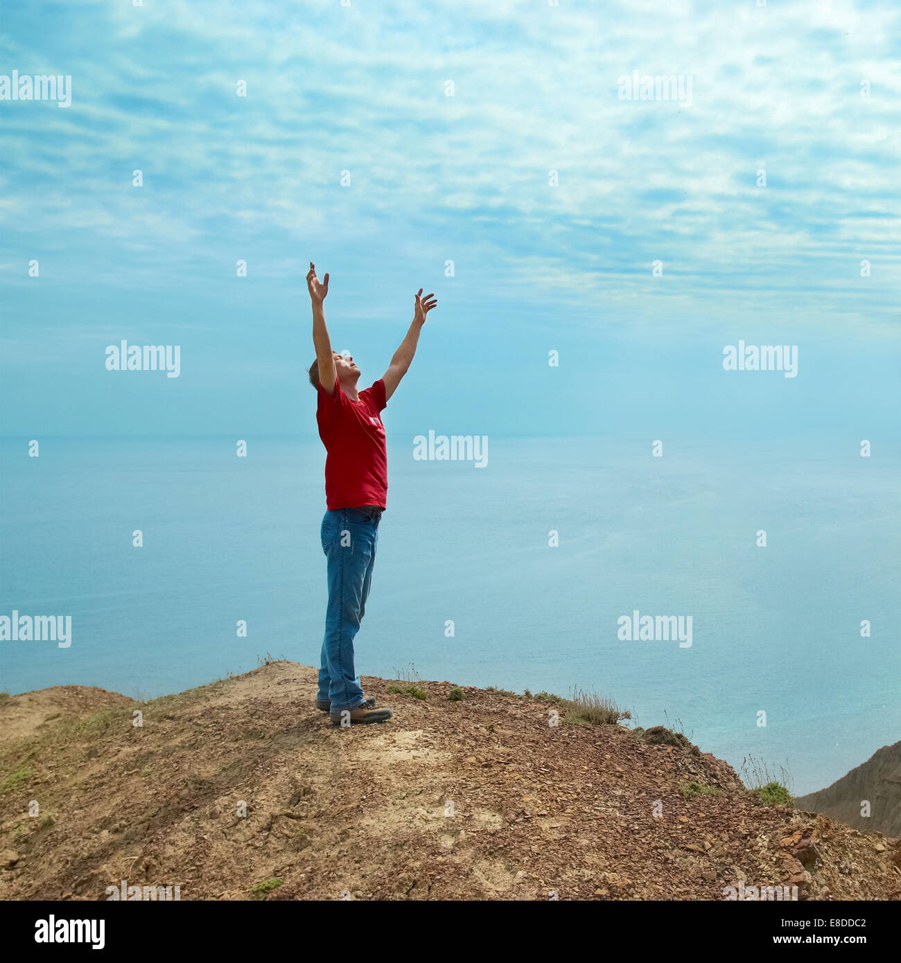 Happy man praying on the cliff with hands up looking at the sea Stock ...