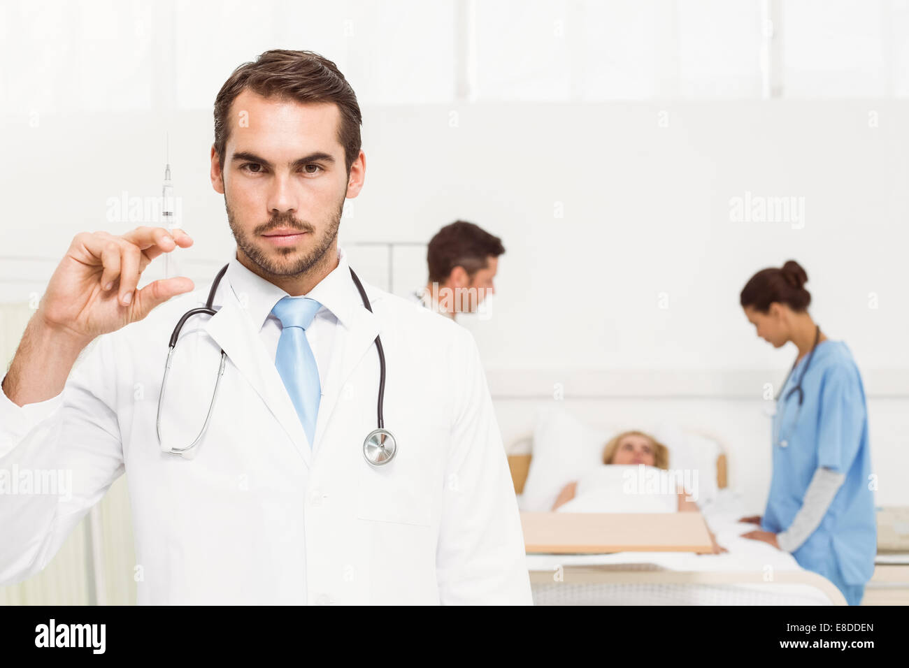 Doctor holding injection with colleagues and patient behind Stock Photo ...