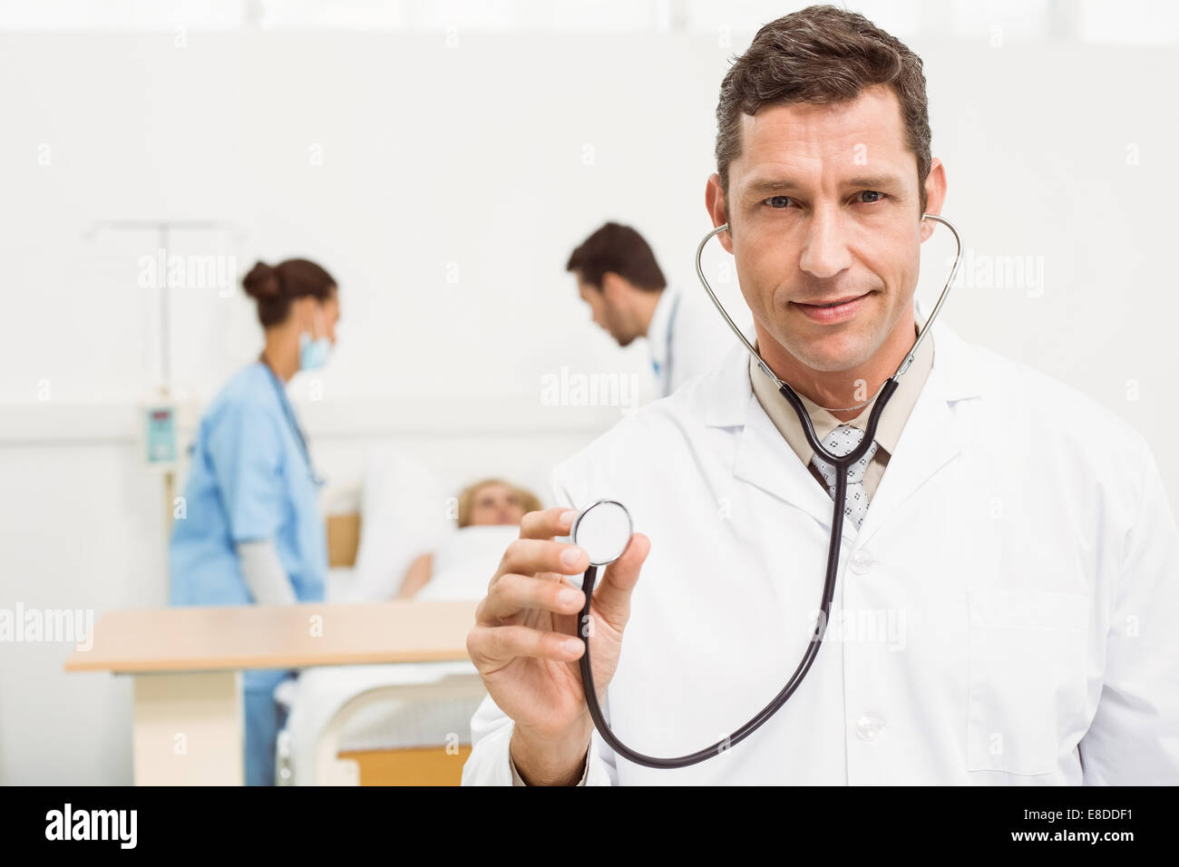 Doctor using stethoscope with colleagues and patient behind Stock Photo ...