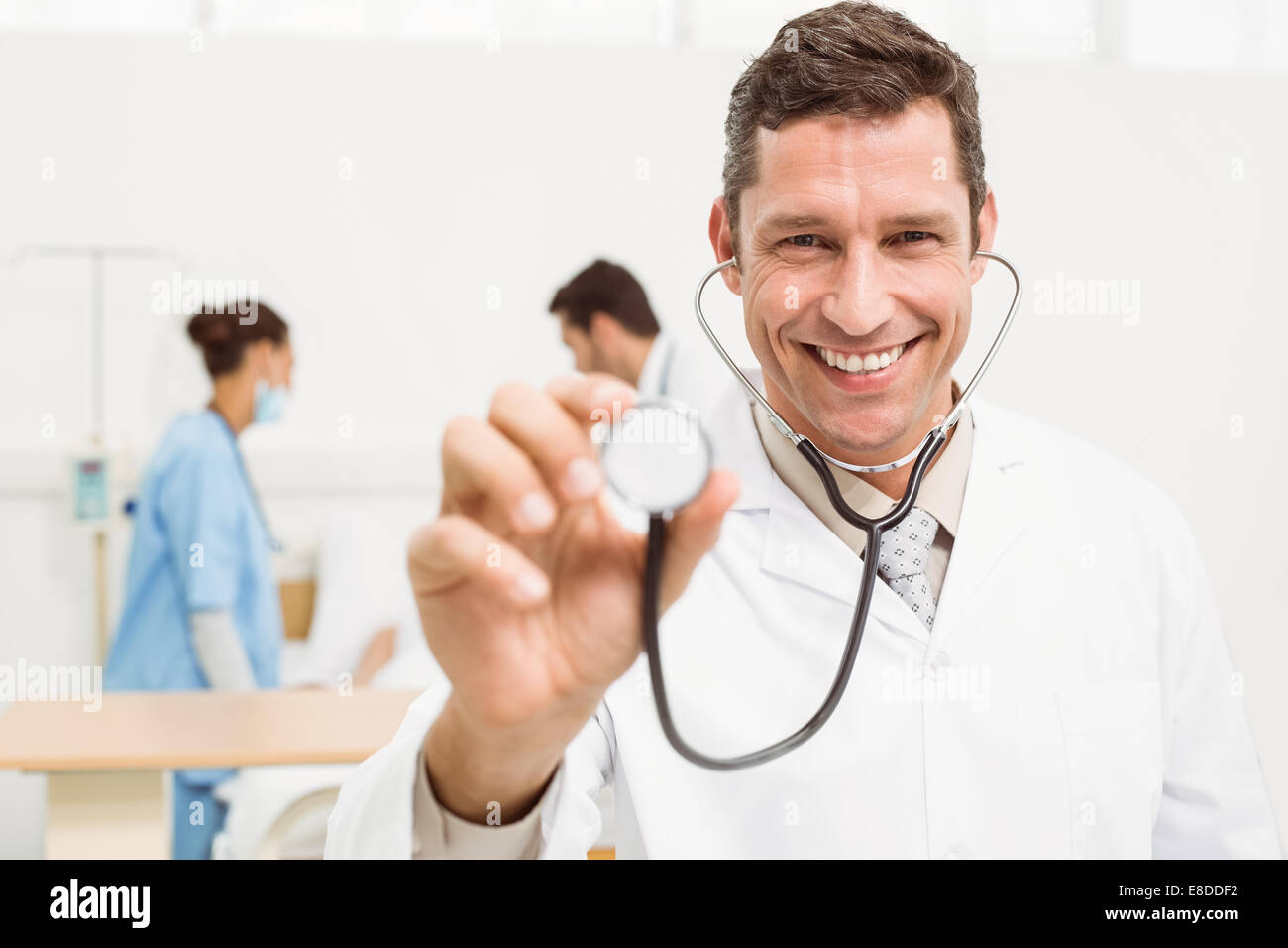 Doctor using stethoscope with colleagues and patient behind Stock Photo ...