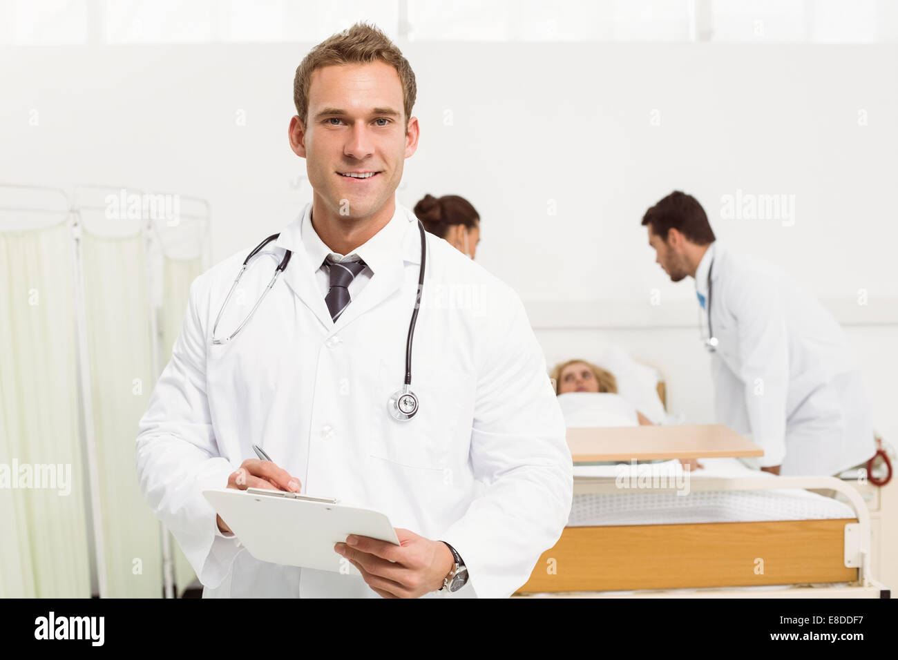 Doctor writing reports with colleague and patient behind Stock Photo ...