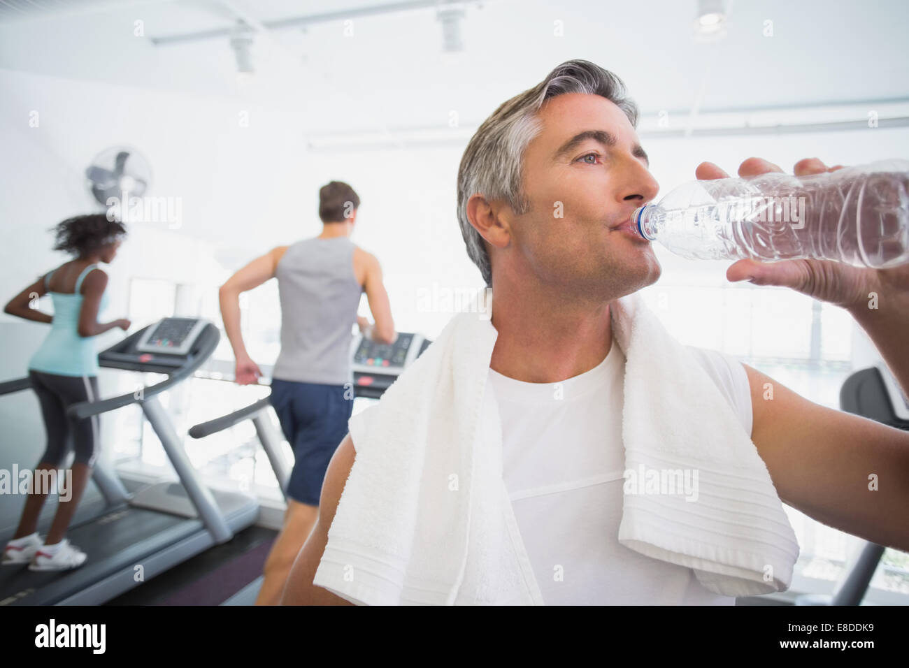 Fit man drinking water beside treadmills Stock Photo - Alamy