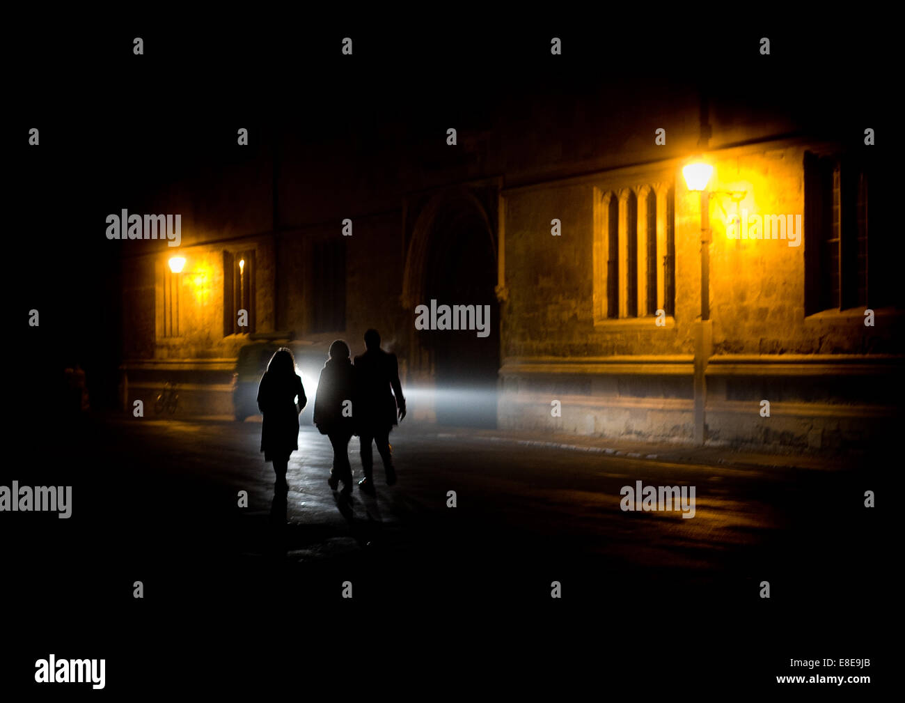 Dramatic silhouette of 3 young people walking towards a car headlight ...