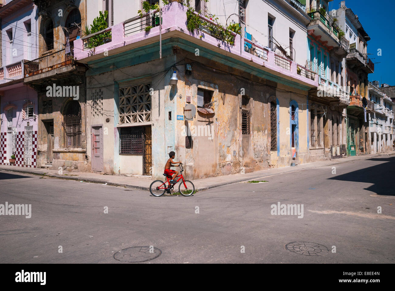 A young Cuban boy riding his bike among run down buildings in the ...