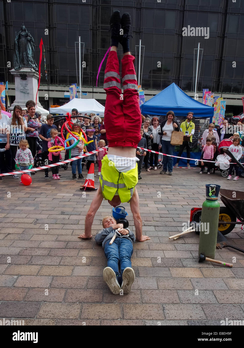 A street performer does a hand stand above a young audience member ...