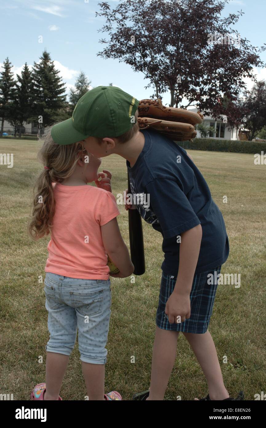 young boy with a baseball bat and glove and bat whispers in a young ...