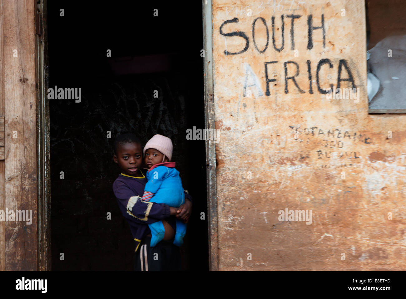 A boy cares for his sibling in the doorway to their home in Dzaleka ...