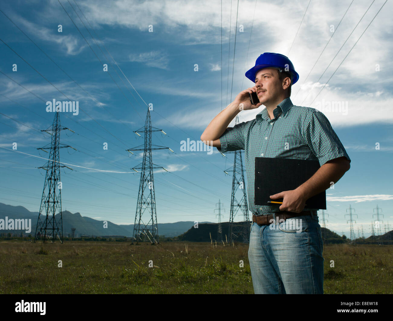 engineer standing on field with electricity towers, talking on the ...