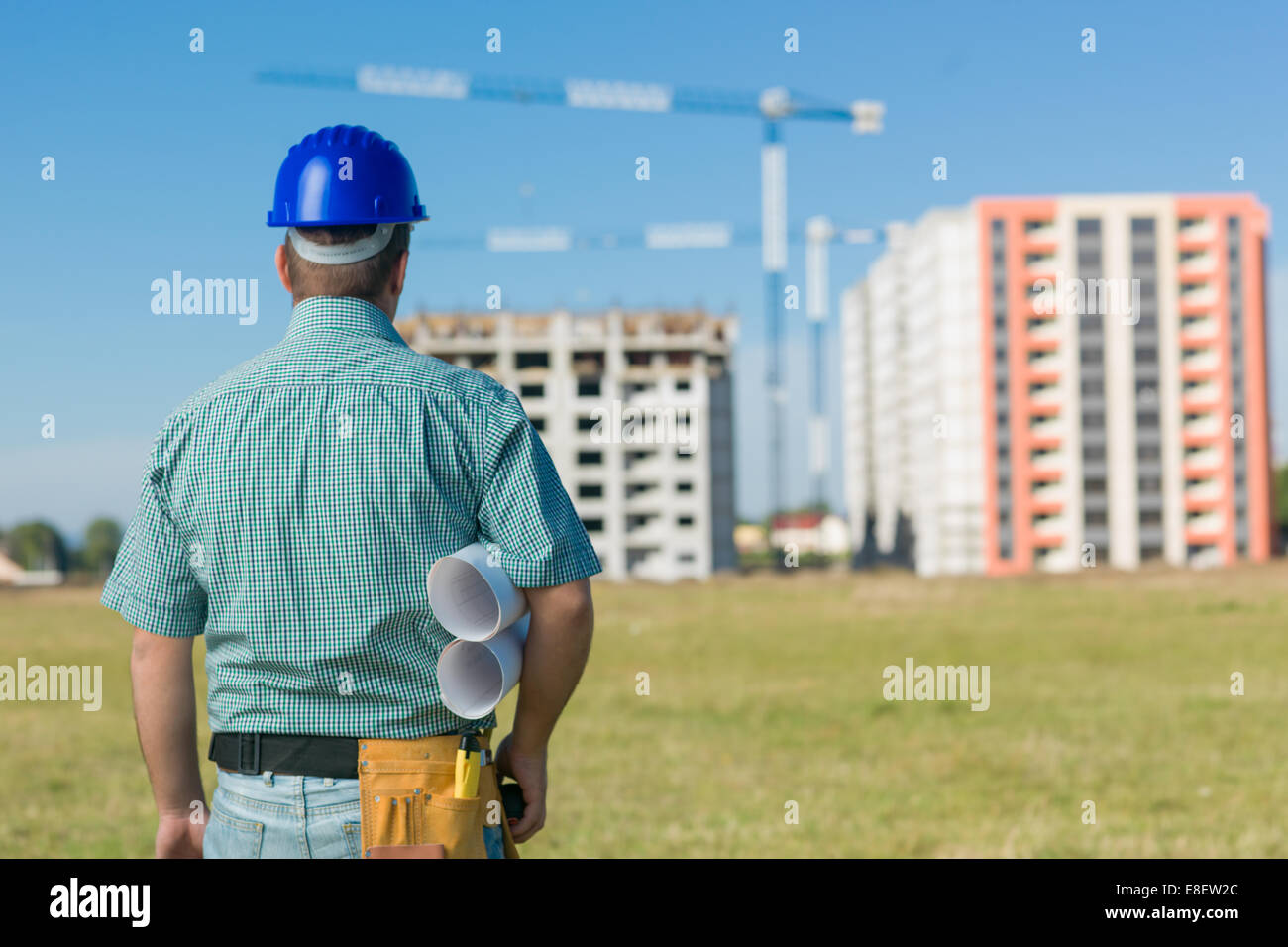 back view of male civil engineer holding plans, looking at building ...