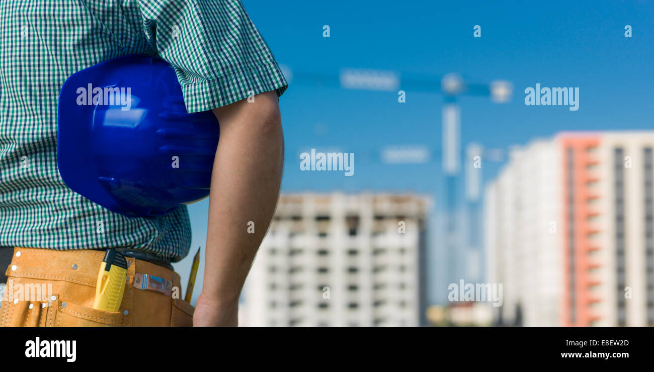 closeup of male engineer holding blue hardhat, with buildings in ...